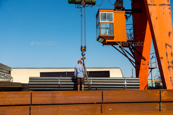 Worker preparing stack of metal pipes for transporting with gantry ...