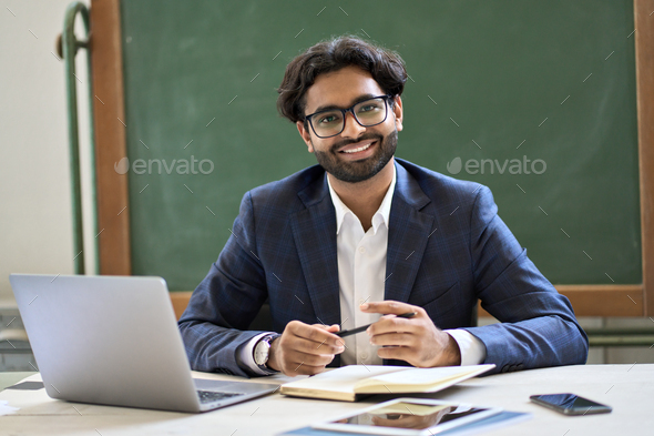 Happy young indian businessman teacher sitting at work in classroom ...