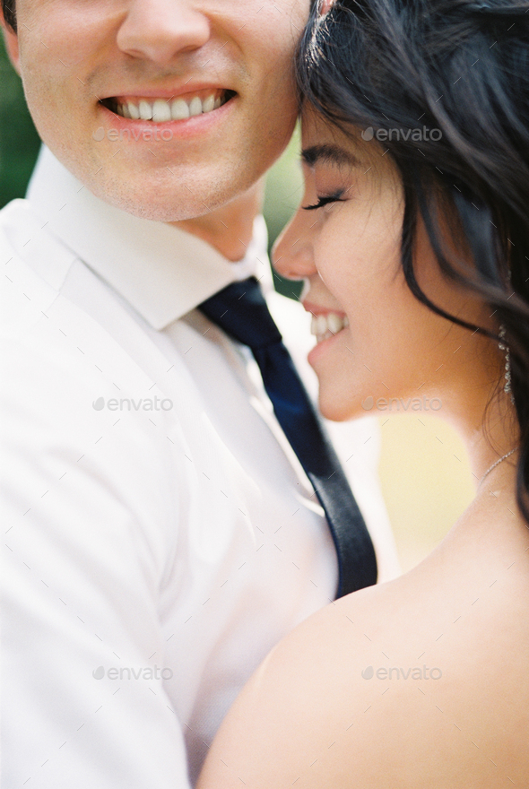 Bride touches her forehead to the cheek of the smiling groom. Cropped ...