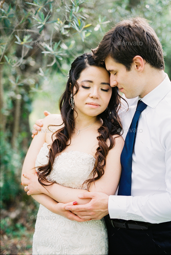 Groom hugs bride, leaning his forehead against her forehead Stock Photo ...