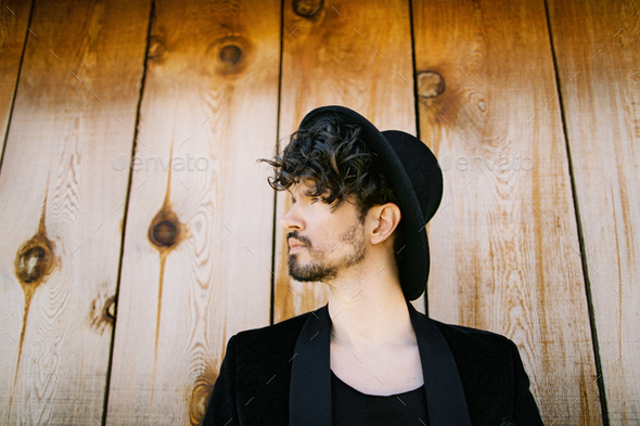 Portrait in profile of a man in a black hat and jacket against a wooden ...