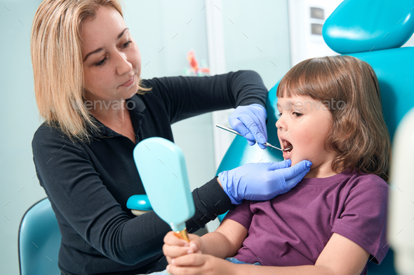 Professional pedodontist examining her young female patient with dental ...