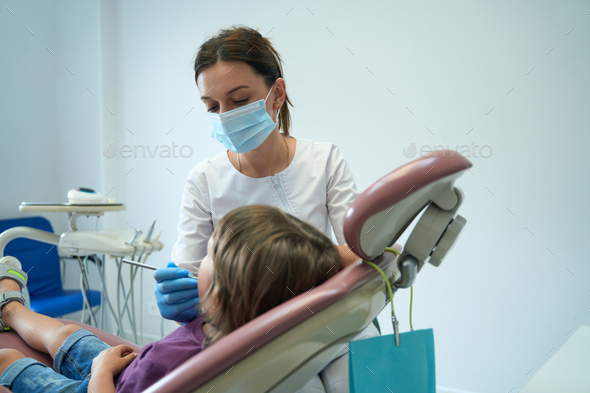 Focused pediatric dentist examining child oral cavity with dental ...