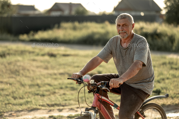 an elderly man rides a bicycle in the village. Grandpa leads a healthy ...