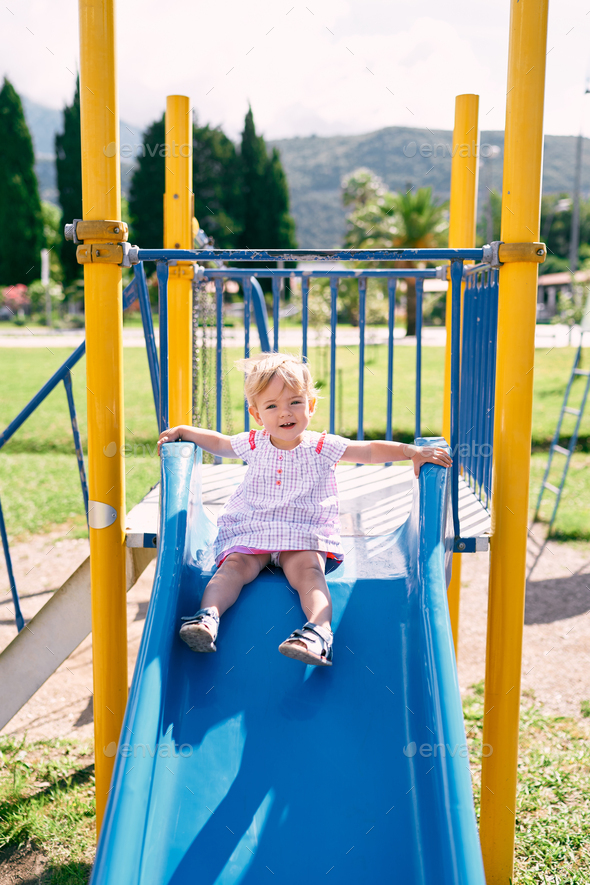Little girl sitting on a slide in the playground, getting ready to ...