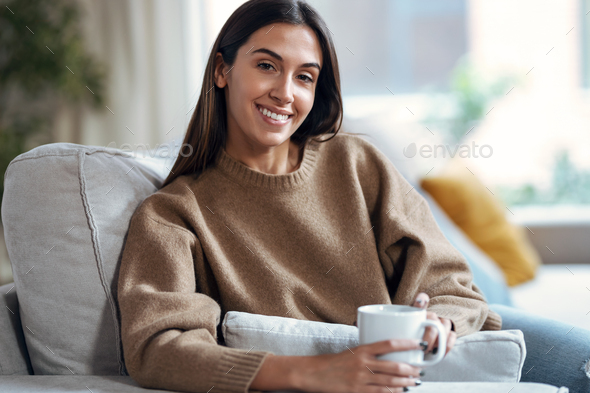 Beautiful young woman drinking a cup of coffee while looking at camera ...