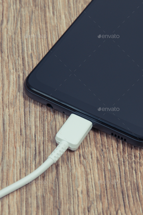 Black smartphone and connected cable of charger. Telephone charging ...