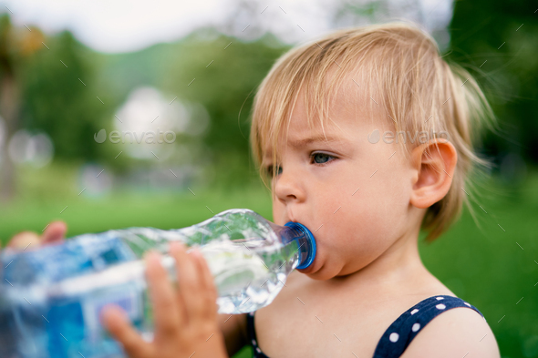 Little girl drinks water from a plastic bottle. Close-up Stock Photo by Nadtochii