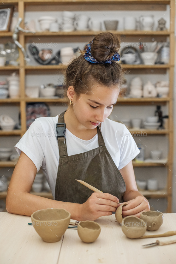 Beautiful teenage girl playing with modeling clay in pottery workshop ...