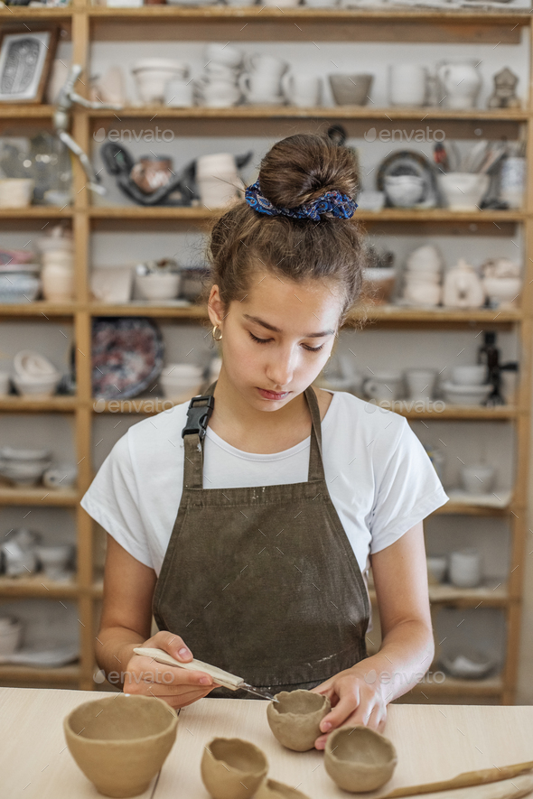 Beautiful teenage girl playing with modeling clay in pottery workshop ...