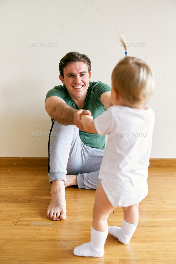 Smiling daddy holding the hands of a little girl Stock Photo by Nadtochii