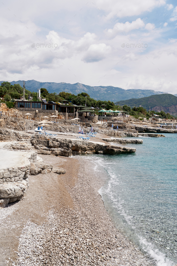 Pebble beach with stone ledges, sun loungers, umbrellas and a small ...