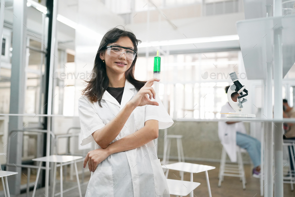 Young scientist in white lab coat working with binocular microscope in the material science lab ...