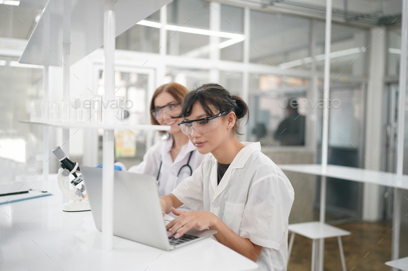 Young scientist in white lab coat working with binocular microscope in ...