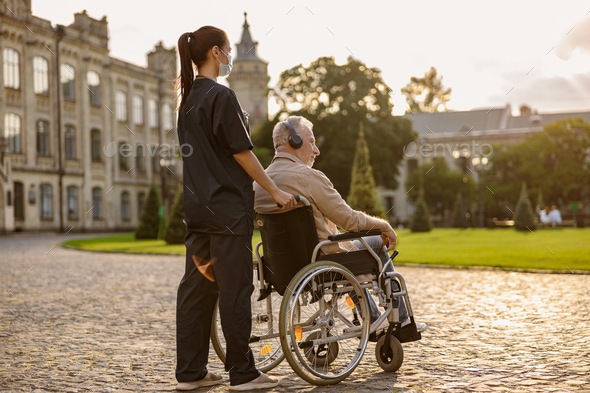 Back view of female care taker in protective mask spending time with ...