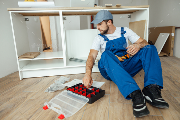 Focused handyman in overalls sitting on the floor while assembling ...
