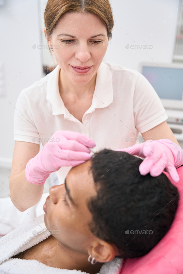 Cosmetologist placing markings on treatment area on young man face ...