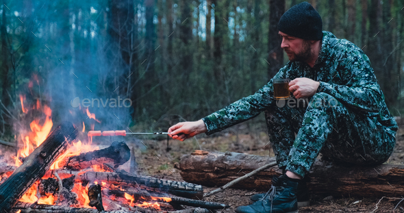 Adult man outdoors is cooking meal on fire. Man roasts sausages on a ...
