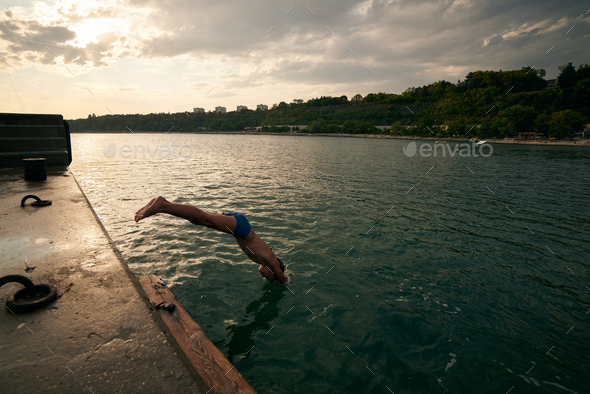 Boy dives into the sea from a pier. Hot summer day. Stock Photo by Sandsun