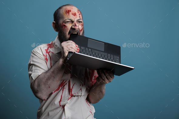 Spooky halloween zombie biting on laptop computer Stock Photo by DC_Studio