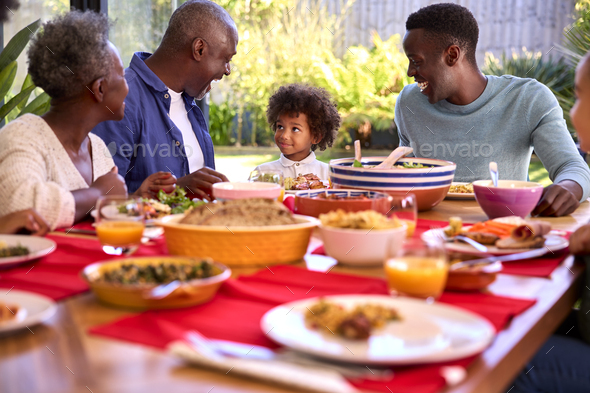 Multi-Generation Family Sitting Around Table At Home Enjoying Meal ...