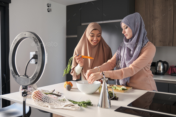 Two muslim food vloggers making a video while prepping vegetables in ...