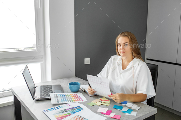 Woman sits at table in modern office next to color palette and fabric ...