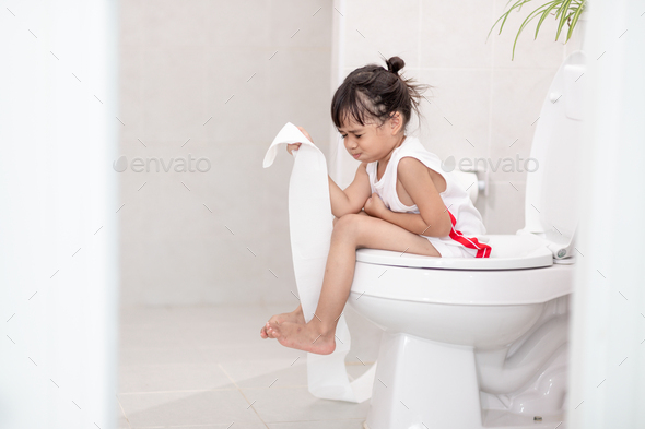 The little girl is sitting on the toilet suffering from constipation or ...
