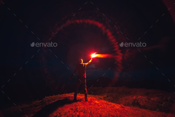The man with a red firework stick standing on a mountain. evening night ...