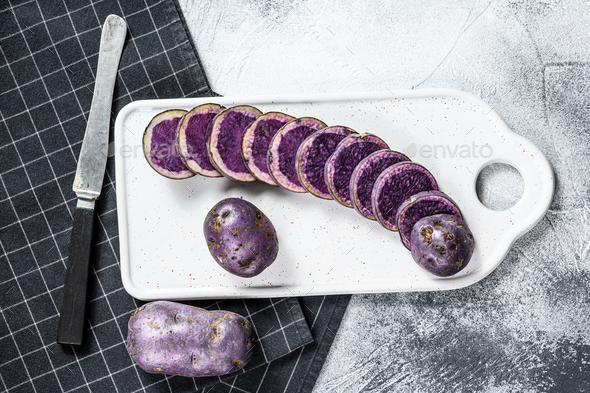 Raw sliced violet potatoes on a white chopping Board. Gray background ...