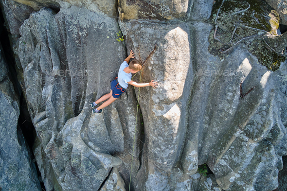 Determined boy climber clambering up steep wall of rocky mountain ...