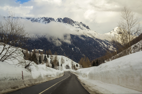 Empty twisty asphalt road stretching through deep snow towards ...