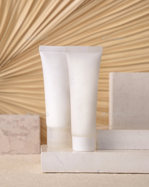 White plastic cream tubes on travertine stone against dry beige palm ...