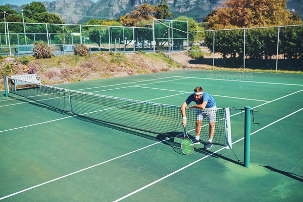 Full length shot of a young male tennis player slouching over the net ...