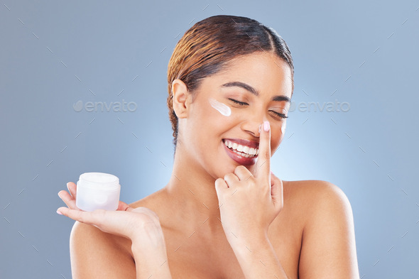 Shot of a young woman applying lotion to her face against a grey ...