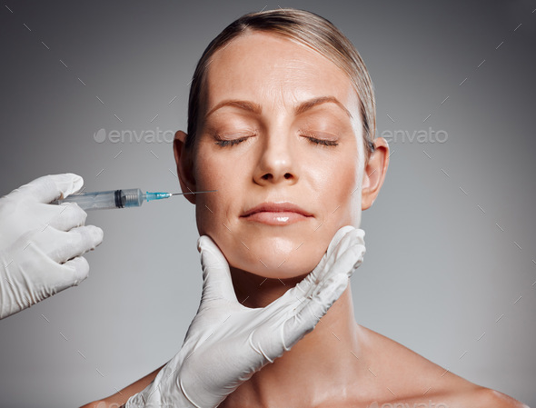 Beautiful mature woman getting botox injection in studio against a grey ...