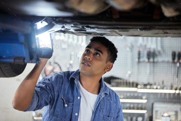 Shot of a handsome young male mechanic working on the engine of a car ...