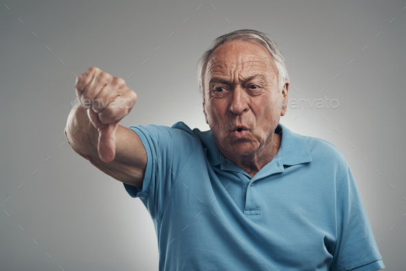 Shot of a unhappy older man giving the thumbs down in a studio against ...
