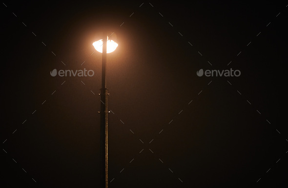 One night lamppost shines with faint mysterious yellow light through ...
