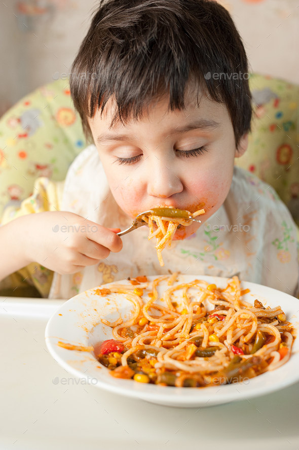 Child eating spaghetti with vegetables. Kid having fun eating. Stock ...