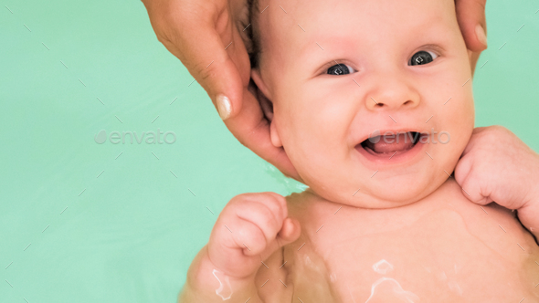Smiling baby is bathing in a large bathtub. Mother teaches a newborn ...
