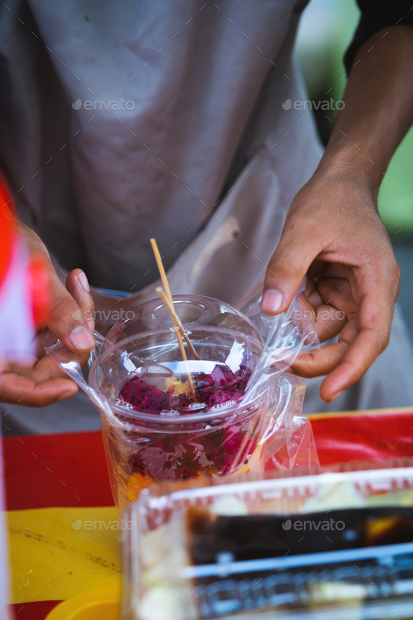 Packing the fresh fruit cuts in a container. Stock Photo by ellinnur