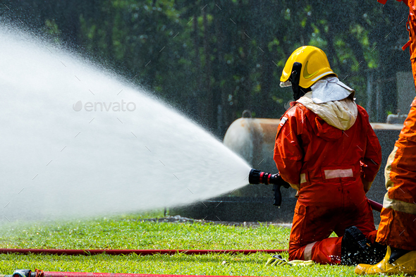 Fire man spray water from hose for fire fighting. Firefighter spraying ...