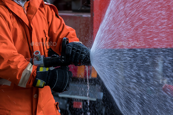 Fire man spray water from hose for fire fighting. Firefighter spraying ...