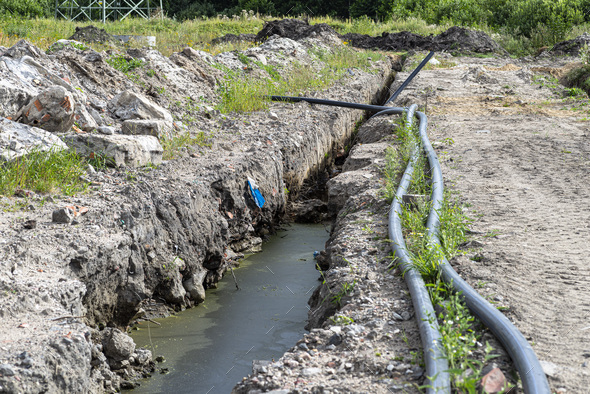 Plastic water pipe lying along the ditch with high groundwater, water ...