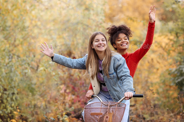 Two young happy diverse female best friends riding bicycle together in ...