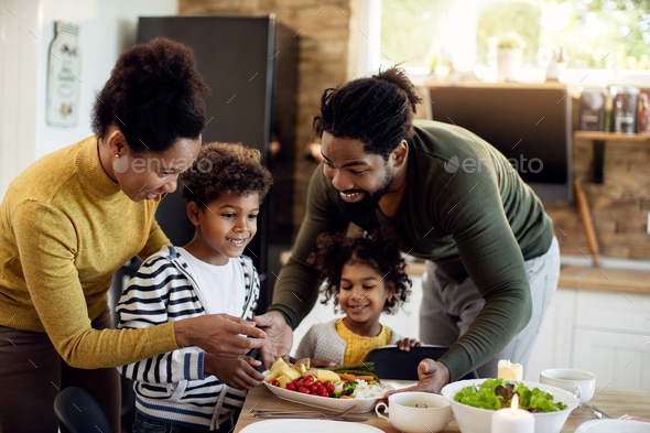 Happy African American family serving food at dining table. Stock Photo ...