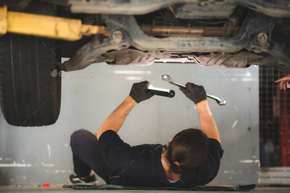 auto car mechanic wearing uniform lying on floor while repairing car ...
