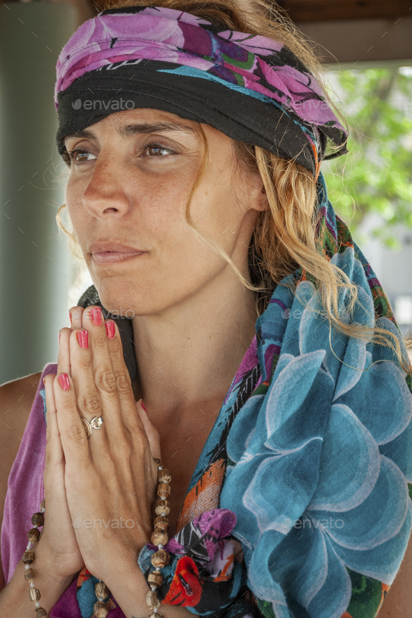 Portrait of a woman clasping hands holding a japa mala and wearing a ...