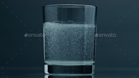 Air bubbles rising glass surface closeup. Acid fluid in transparent cup ...